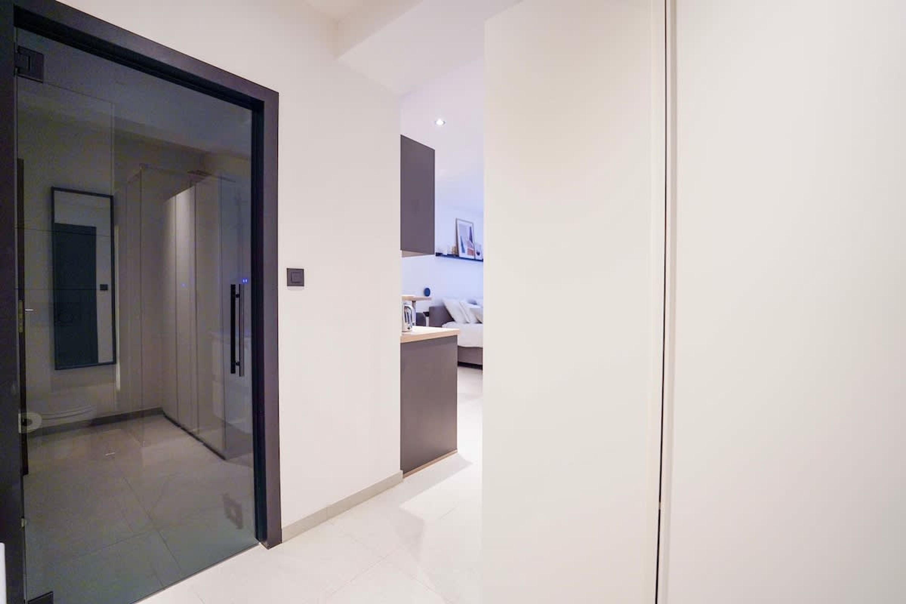 Interior moderno com porta de vidro que dá para um quarto, área de cozinha com bancada e parede branca.