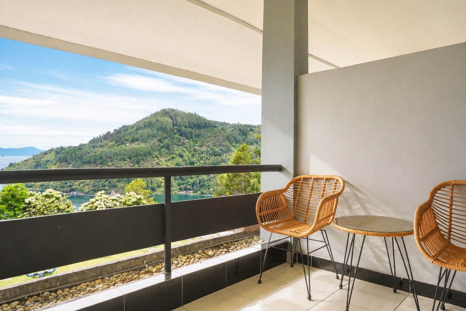Varanda com vista para montanha e lago, duas cadeiras de vime e piso de azulejos.
