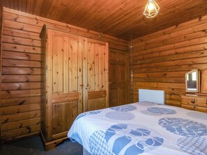 Quarto de cabana de madeira com uma cama, um guarda-roupa e um espelho.