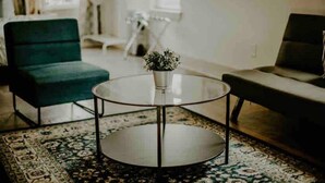 Uma sala de estar moderna com uma mesa de centro redonda de vidro, uma poltrona verde e um sofá.