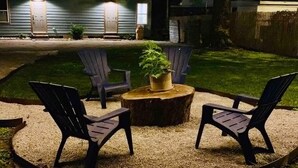 Um quintal com uma área de estar circular, duas cadeiras Adirondack, uma planta em vaso e uma guirlanda de luzes.