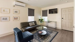 Uma sala de estar com sofá, mesa de centro, televisão e quadros nas paredes.