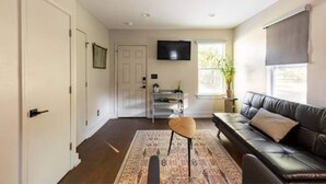 Uma sala de estar com sofá, televisão, porta e janela com uma planta.