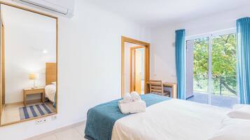 Quarto de hotel com cama, escrivaninha, cadeira, espelho e varanda com cortinas.