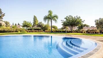 Piscina límpida com borda azulejada, rodeada por um deck de madeira e vegetação.