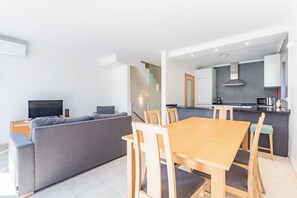 Uma sala de estar moderna com um sofá, uma mesa de jantar de madeira e uma área de cozinha com armários e um fogão.