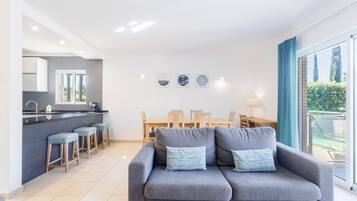 Uma sala de estar moderna com um sofá cinzento, uma área de cozinha com balcão e um conjunto de jantar.