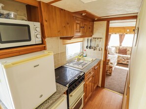 Cozinha compacta com micro-ondas, fogão, pia e armários de madeira.