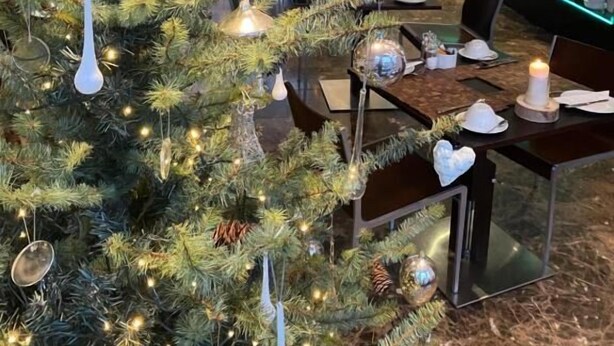 Uma sala de jantar moderna com um pinheiro de Natal, mesas postas para refeições e um bar com prateleiras cheias de garrafas.