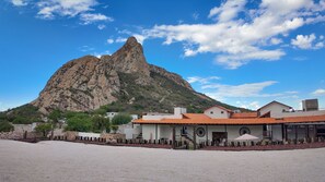 Um edifício com telhado de telhas vermelhas, fachada branca e uma montanha imponente ao fundo.