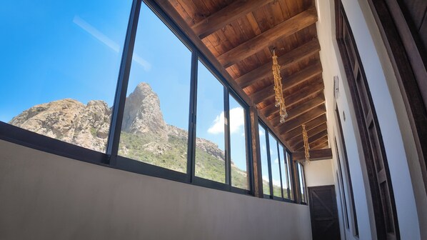 Quarto com grandes janelas, vigas de madeira no teto e vista para uma montanha.