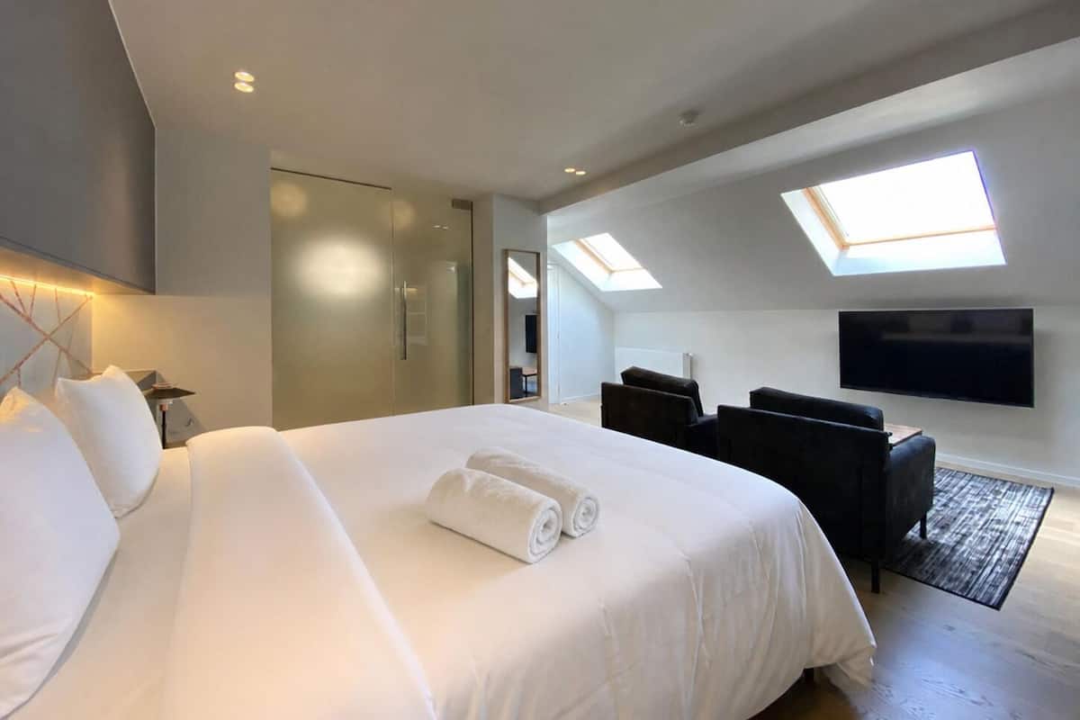 Quarto de hotel moderno com uma cama grande, área de estar e claraboias.