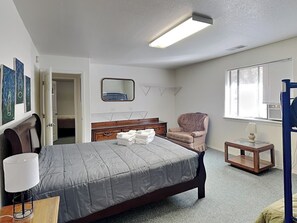 Quarto com cama, cadeira, mesa de cabeceira, espelho e janela com persianas.