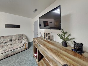 Uma sala de estar com televisão de tela plana na parede, mesa de centro de madeira, sofá, planta em vaso e uma figura de urso.
