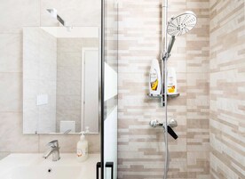 Uma casa de banho moderna com cabine de duche em vidro, lavatório com dispensador de sabonete e espelho.