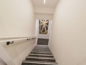 Uma escadaria com corrimão, degraus carpetados e uma obra de arte pendurada na parede.