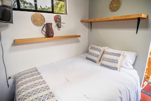 Quarto com cama, almofadas, mesa de cabeceira e prateleiras fixadas na parede.