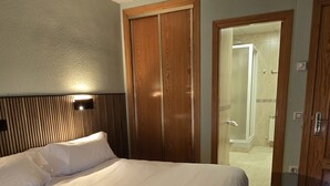Quarto de hotel com uma cama grande, cabeceira de madeira, um closet espaçoso e área de chuveiro.