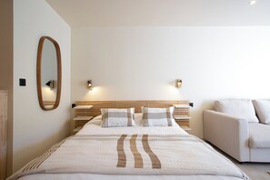 Quarto com cama, abajures, espelho e sofá.