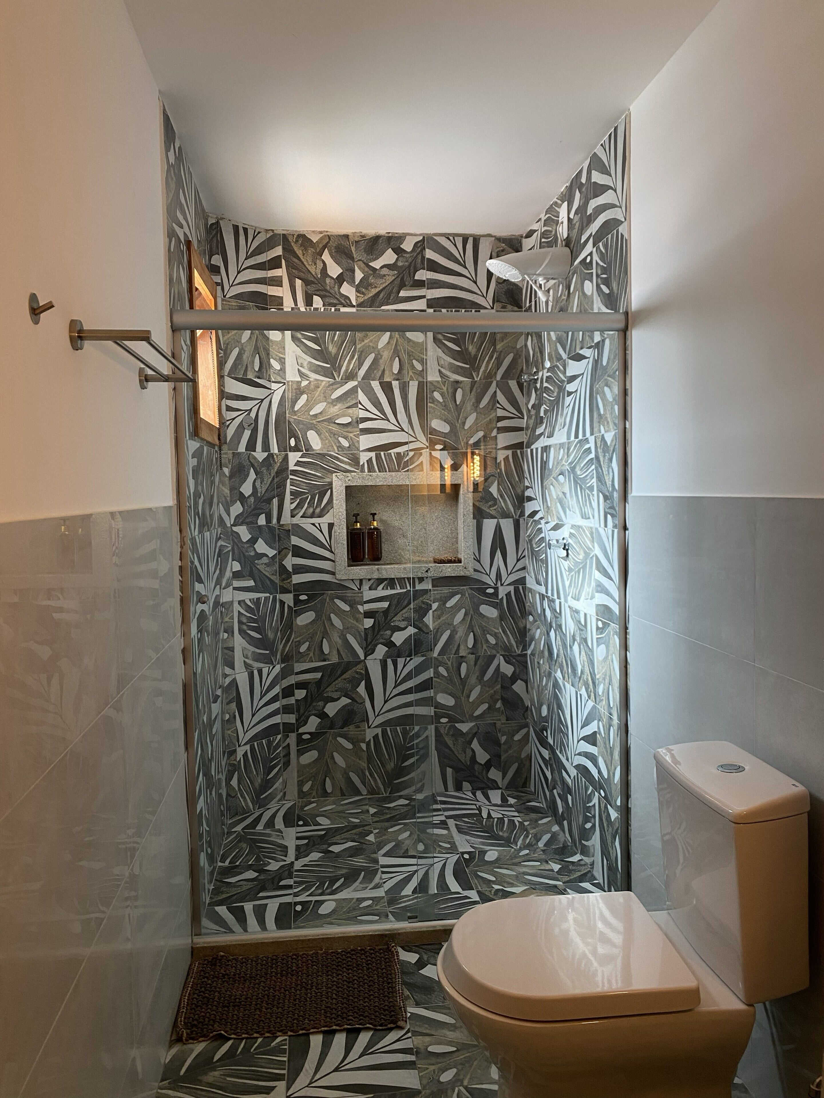 Um chuveiro com porta de vidro, um vaso sanitário e uma prateleira com artigos de higiene pessoal.