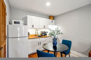 Uma cozinha compacta com armários brancos, micro-ondas, cafeteira e uma mesa de jantar com cadeiras azuis.