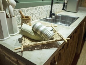 Uma bancada de cozinha com uma cesta trançada contendo uma toalha listrada, um porta-utensílios e uma pia.