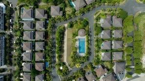 Vista aérea de um bairro residencial com várias casas, uma piscina central e áreas verdes ao redor.