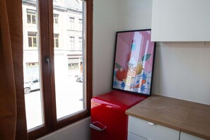 Um quarto com um armário vermelho, uma janela com vista para edifícios e um quadro na parede.