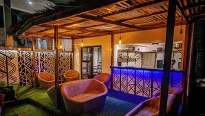 Uma área de estar acolhedora, com cadeiras de vime, um bar e uma cozinha ao fundo.