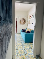 Um corredor leva a uma sala de estar com piso estampado, um sofá azul-turquesa e uma obra de arte pendurada na parede.