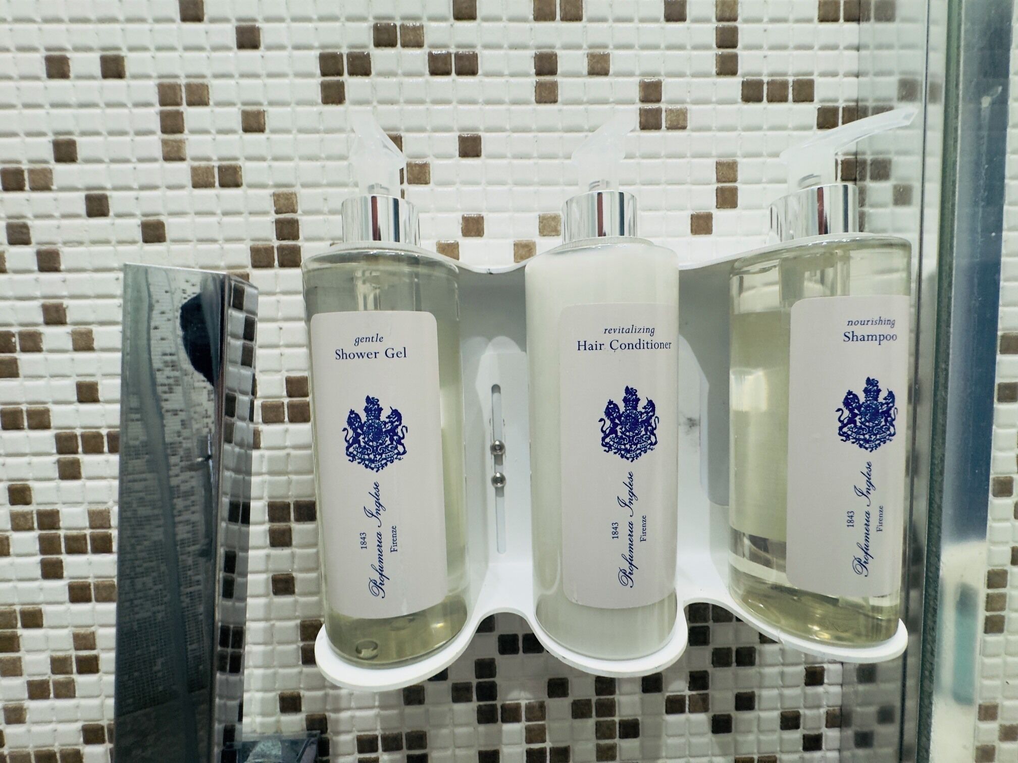 Casa de banho com painel de azulejos e três frascos de produtos para cabelo num suporte.