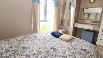 Quarto com colcha florida, mesa de cabeceira, cadeira, guarda-roupa e espelho.