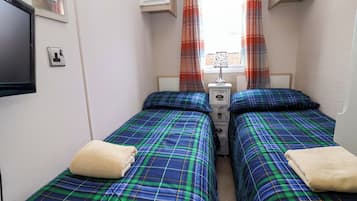 Quarto pequeno com duas camas, uma mesa de cabeceira, um espelho e uma janela com cortinas.