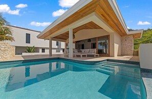 Uma casa moderna com piscina, um alpendre coberto e uma parede de pedra.