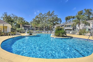 Piscina com água azul cristalina, rodeada por espreguiçadeiras e palmeiras.