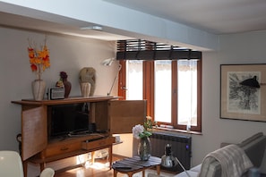 Sala de estar com unidade de entretenimento de madeira, televisão, mesa de centro e janela com persianas.