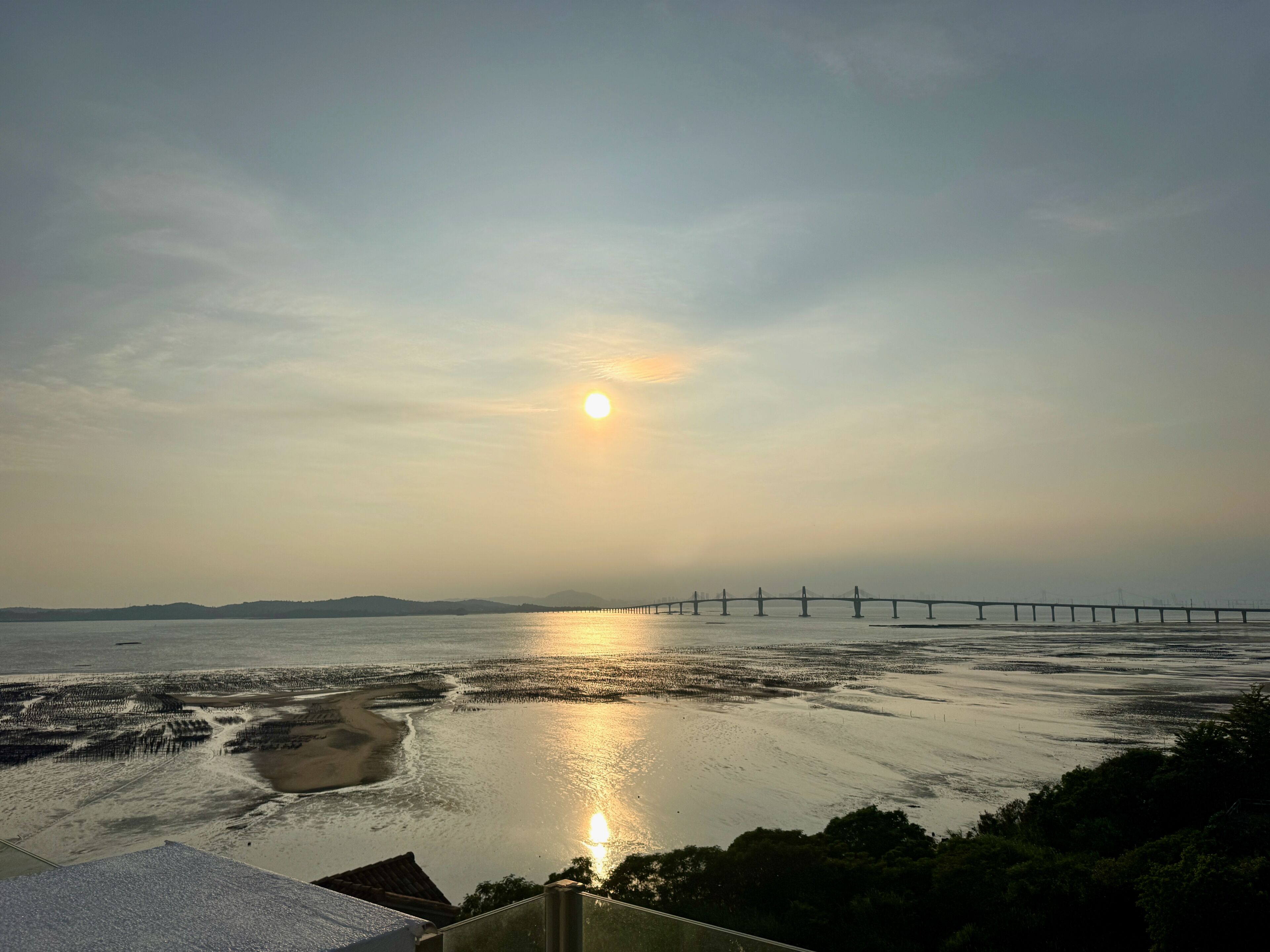Um pôr do sol sobre uma ponte, com uma praia ao primeiro plano.