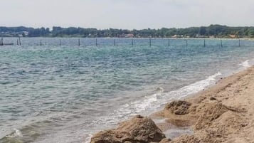 Uma praia com águas cristalinas, areal arenoso e uma linha de árvores ao longe.