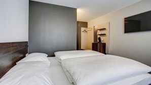 Quarto de hotel com cama, guarda-roupa, espelho e televisão.
