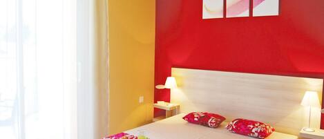 Quarto de hotel com cama, mesa de cabeceira, luminária, bandeja com comida e janela com cortinas.