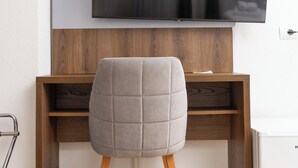Quarto moderno com escrivaninha de madeira, cadeira acolchoada cinza e televisão de tela plana na parede.