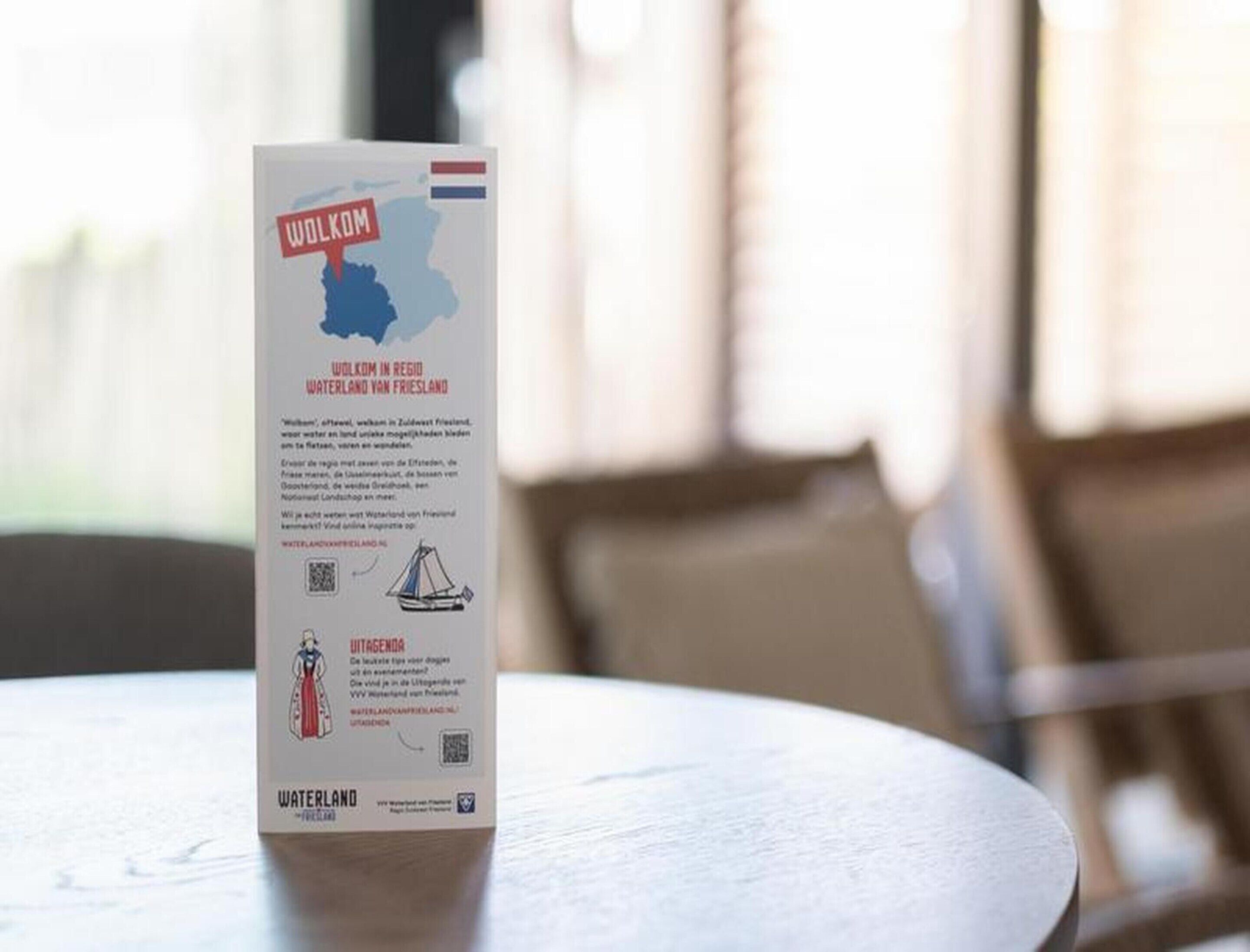 Um folheto sobre uma mesa com um mapa de WILKOM, texto sobre WATERLAND VAN FRIESLAND e um código QR.