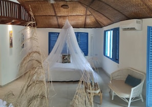 Quarto com cama sob toldo, uma cadeira de vime e um ventilador de teto.