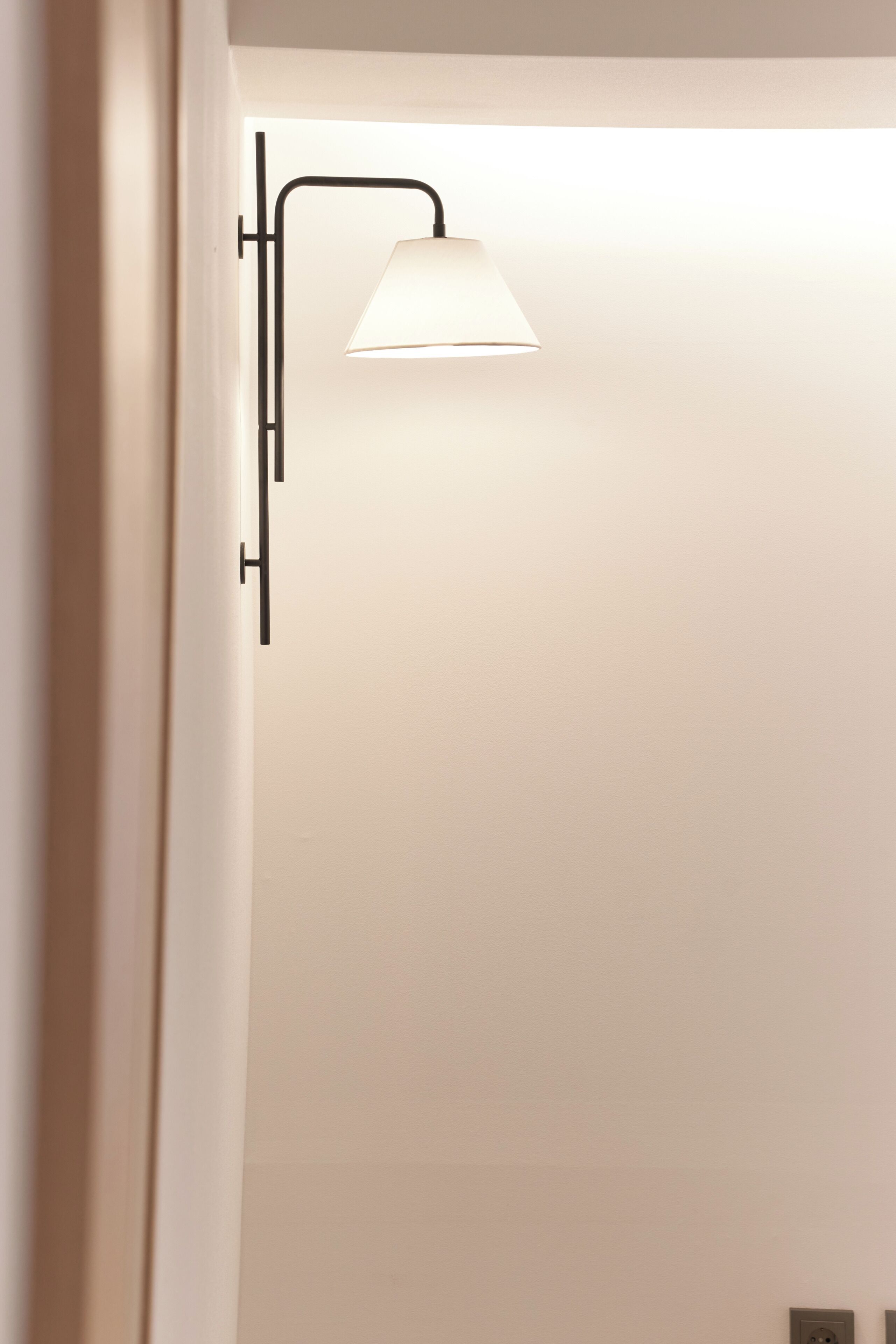 Casa de banho moderna com design minimalista, com um candeeiro fixado na parede e área de duche visível.