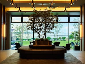 Um lobby moderno com uma grande árvore em vaso, área de estar e amplas janelas com vista para o exterior.