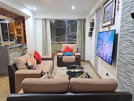 Uma sala de estar com sofá, mesa de centro, televisão e parede com textura de pedra.