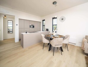Uma cozinha moderna com uma ilha central, uma área de jantar com mesa redonda e um espaço de estar com sofá.