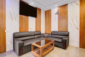 Uma sala de estar moderna com um sofá seccional, uma mesa de centro de vidro, paredes revestidas de madeira e uma TV de tela plana montada acima do sofá.
