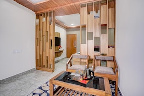 Quarto moderno com divisórias de madeira, uma mesa de centro de vidro com bandeja, duas poltronas acolchoadas e uma porta de madeira.