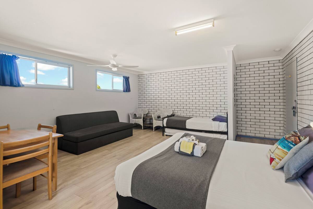 Quarto moderno com cama, sofá, mesa de jantar e janela com cortinas.